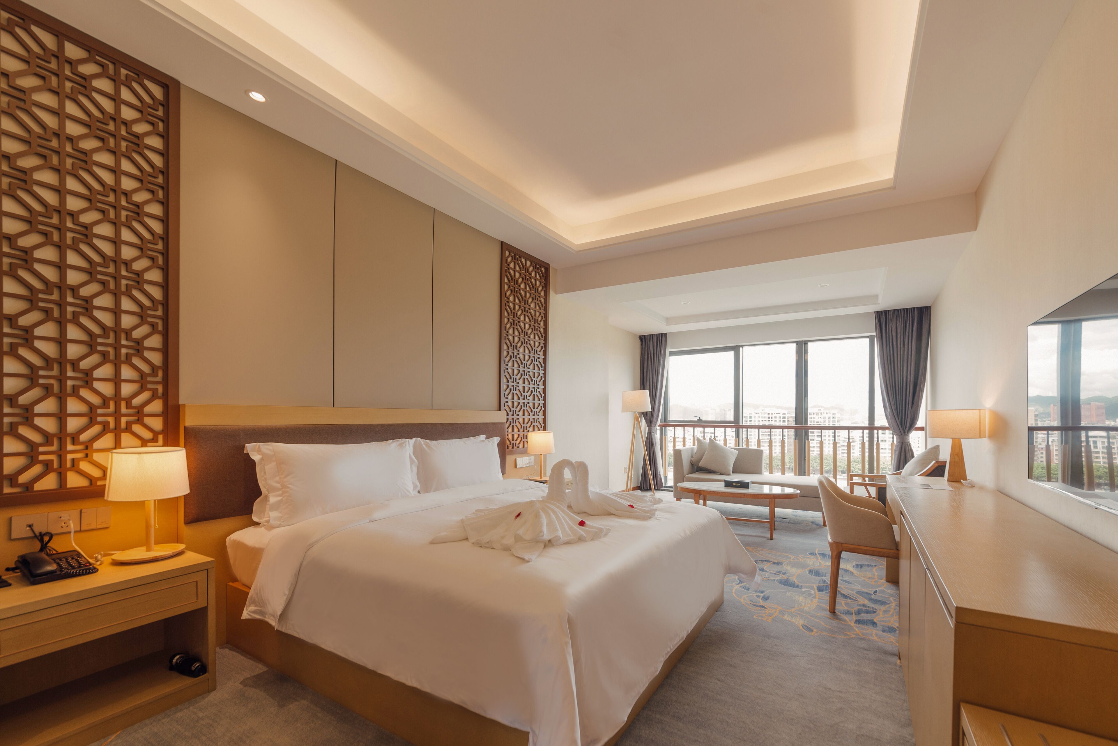 Quarto de hotel com uma cama grande, uma escrivaninha, uma cadeira, um sofá e uma varanda com vista.
