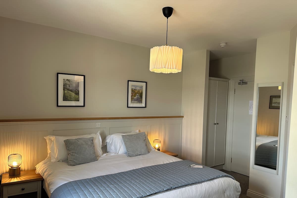 Quarto bem arrumado com cama grande, abajures e quadros nas paredes.