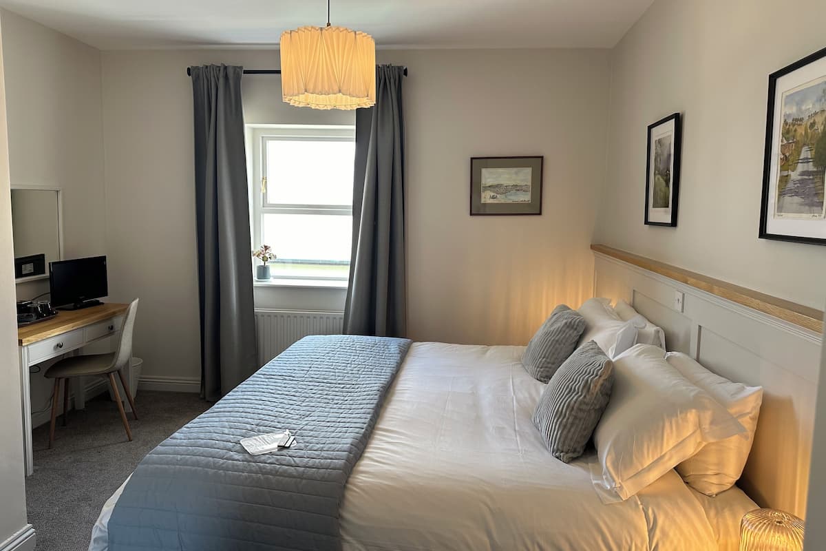 Quarto com cama, escrivaninha e janela com cortinas.