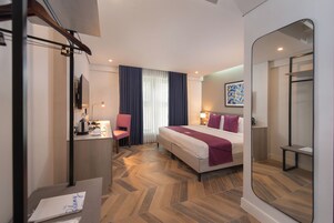 Quarto de hotel moderno com uma cama grande, uma escrivaninha com cadeira, um espelho e uma televisão.