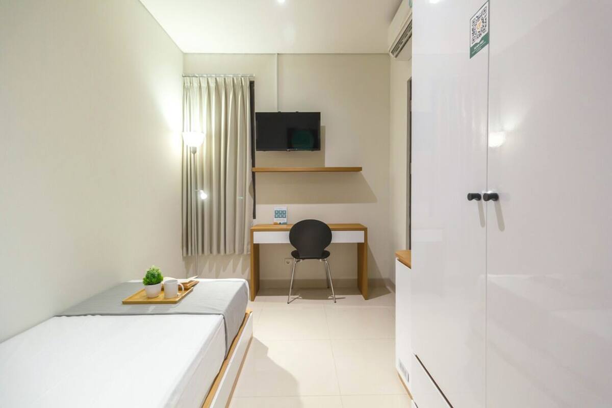 Quarto de hotel com cama, escrivaninha com cadeira, televisão na parede e guarda-roupa.