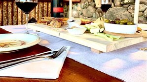 Uma mesa posta com uma garrafa de vinho, copos, pratos com comida e um fundo de parede de pedra.