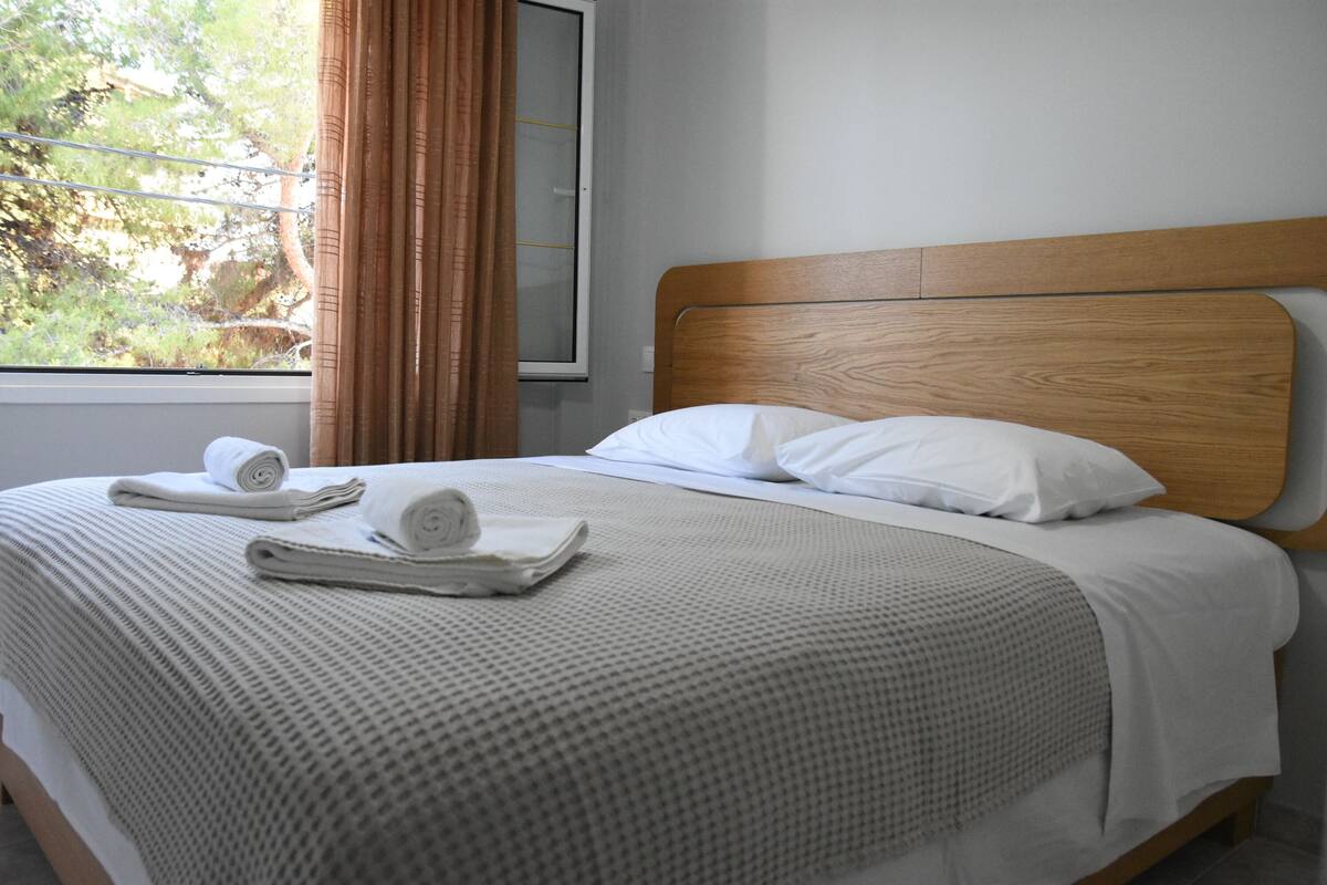 Uma cama bem arrumada com cabeceira de madeira, roupa de cama branca e uma toalha enrolada ao lado.