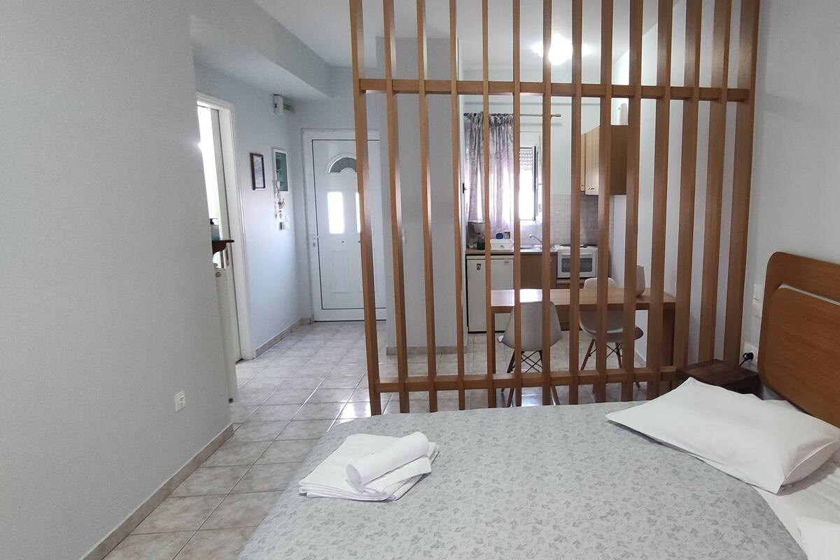 Quarto com cama, cabeceira de madeira, uma escrivaninha com cadeira e um divisório.