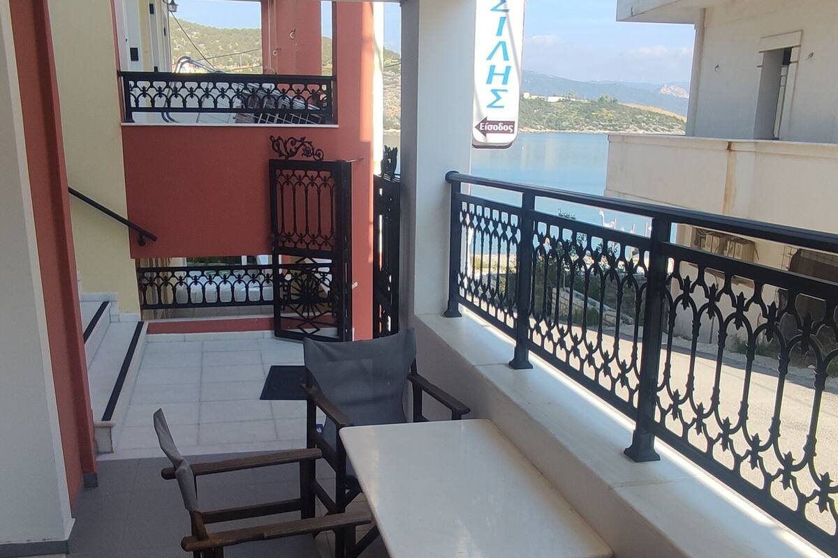 Varanda com mesa, cadeiras, grade e vista para um edifício e paisagem.