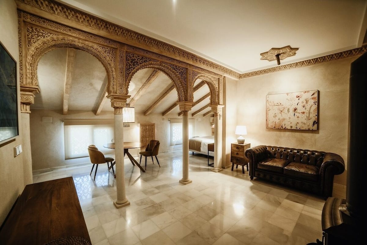 Um quarto espaçoso com teto alto, arcos elaborados, um sofá de couro, uma mesa de jantar e uma grande janela que proporciona luz natural.