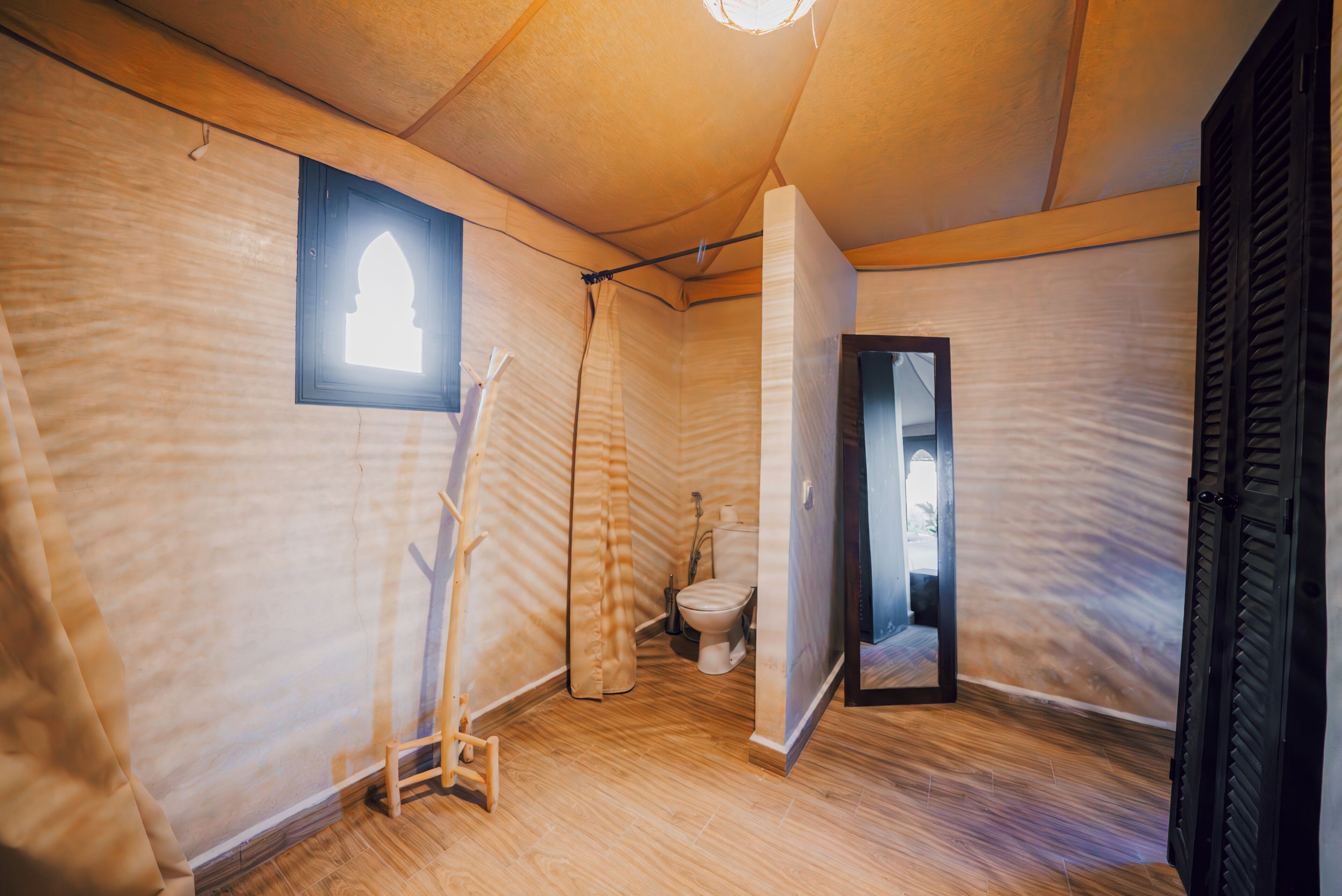Quarto com paredes e chão de madeira, um vaso sanitário, uma escada de madeira e uma porta que dá para outro cômodo.