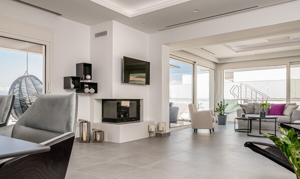Uma sala de estar ampla com design moderno, com lareira, disposição de assentos e grandes janelas com vista para o exterior.