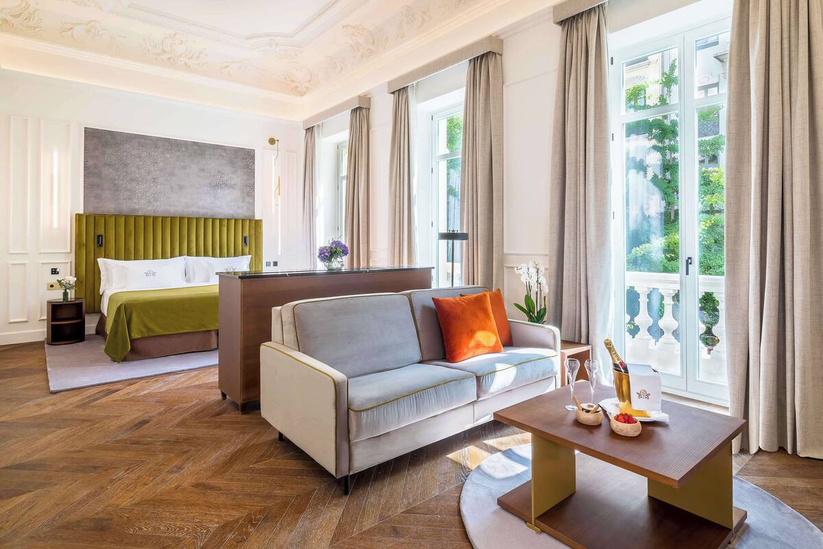 Quarto de hotel com cama, sofá, mesa de centro e vista para o verde lá fora.