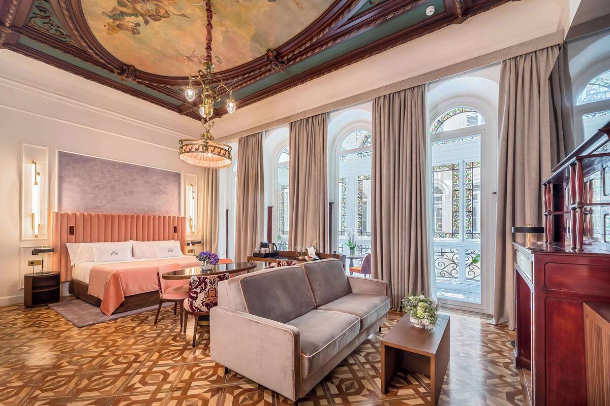Quarto de hotel com uma cama grande, um sofá, uma mesa de jantar e um candelabro.