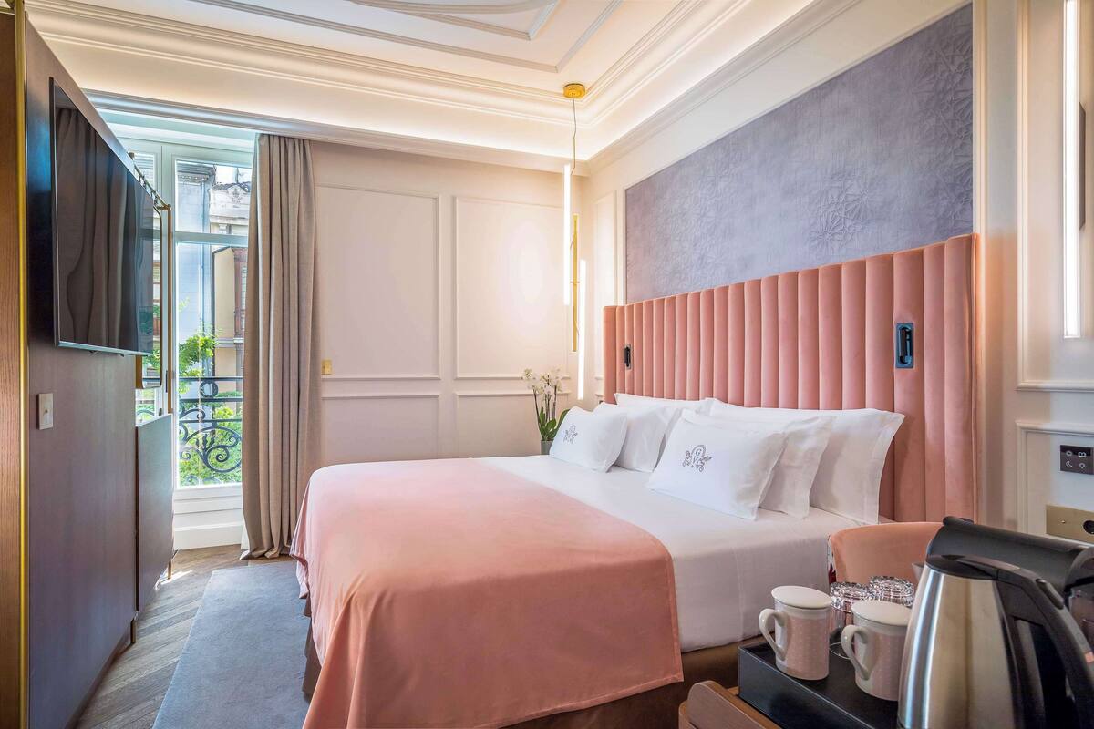 Quarto de hotel com uma cama grande, televisão, máquina de café e vista para o exterior.