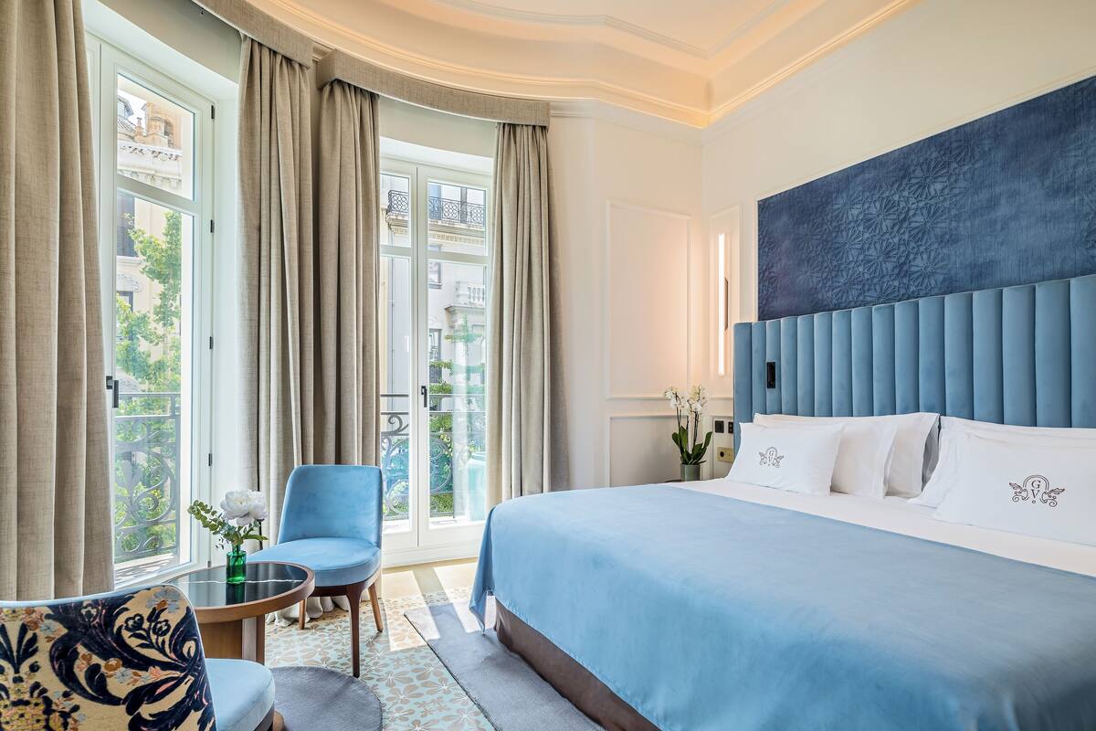 Quarto de hotel com uma cama grande, uma cadeira, uma mesinha e vista para o exterior.