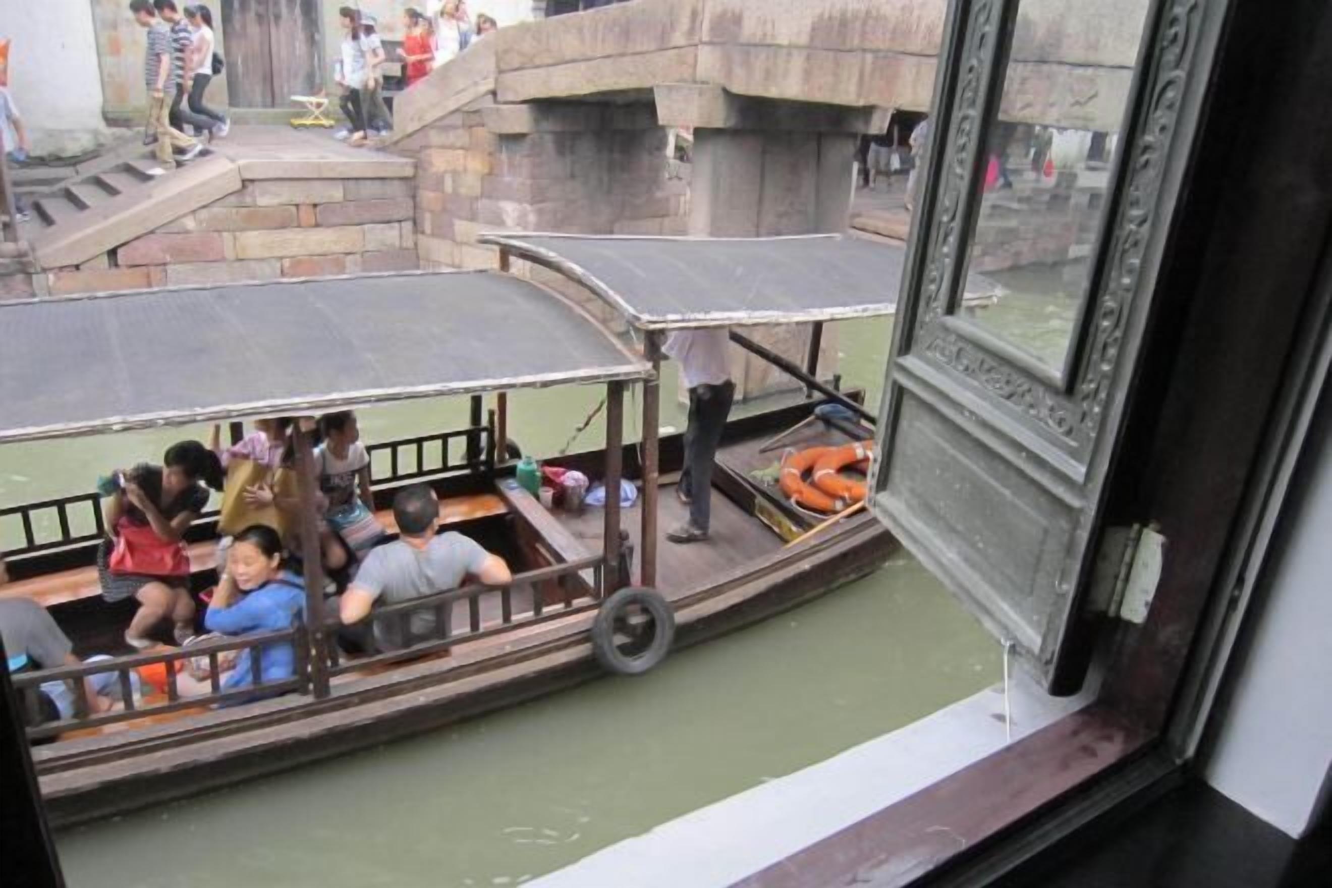 Um barco com passageiros, uma estrutura de pedra ao fundo e uma janela com vista.