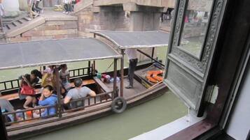 Um barco com passageiros, uma estrutura de pedra ao fundo e uma janela com vista.