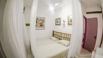 Quarto com duas camas, paredes brancas e uma porta à direita.