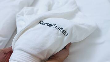Uma mão segurando um travesseiro branco com a inscrição 'Kertel Suites'.