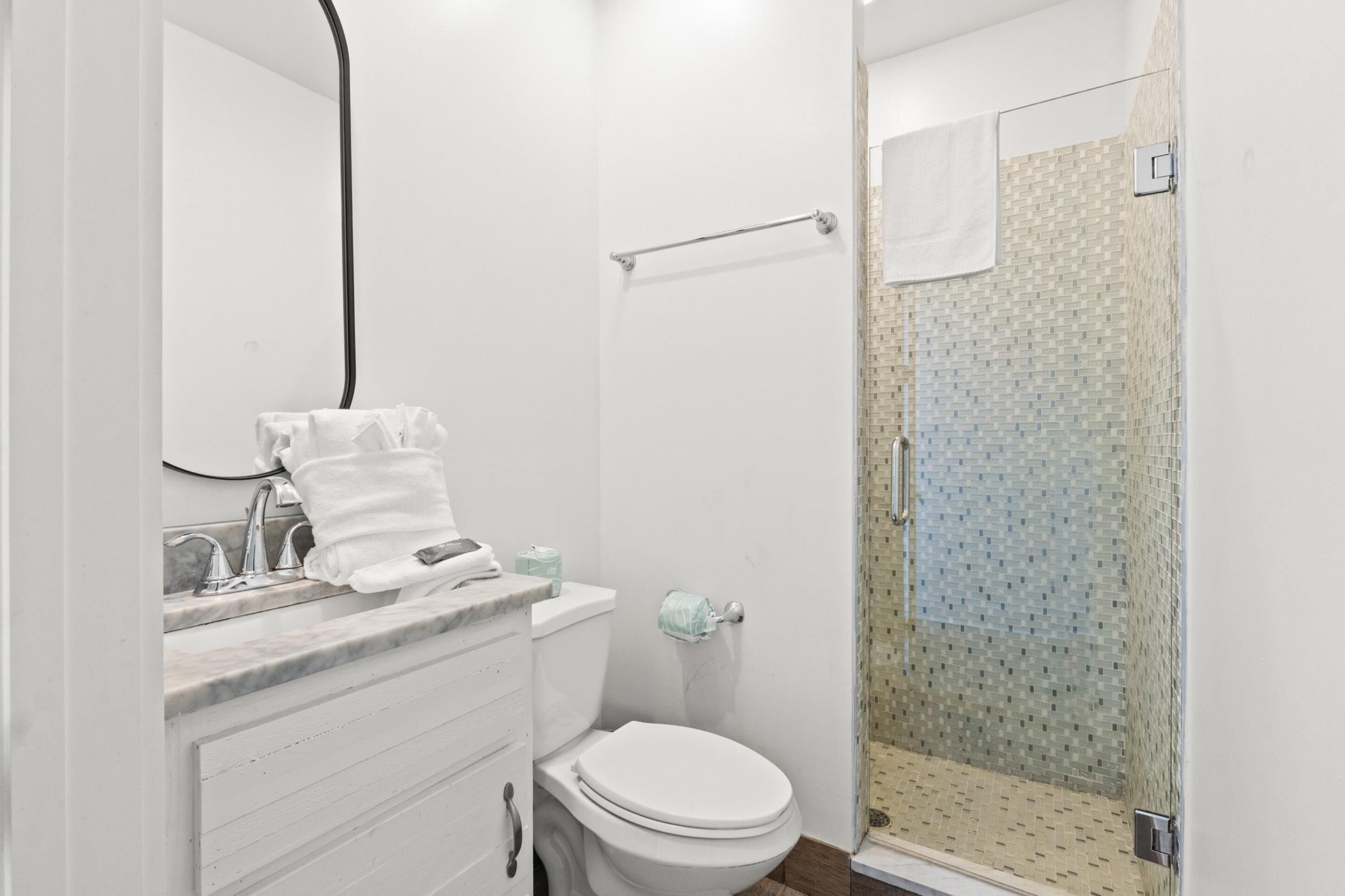 Um banheiro com vaso sanitário branco, pia com bancada de mármore, porta-toalhas e chuveiro com porta de vidro.