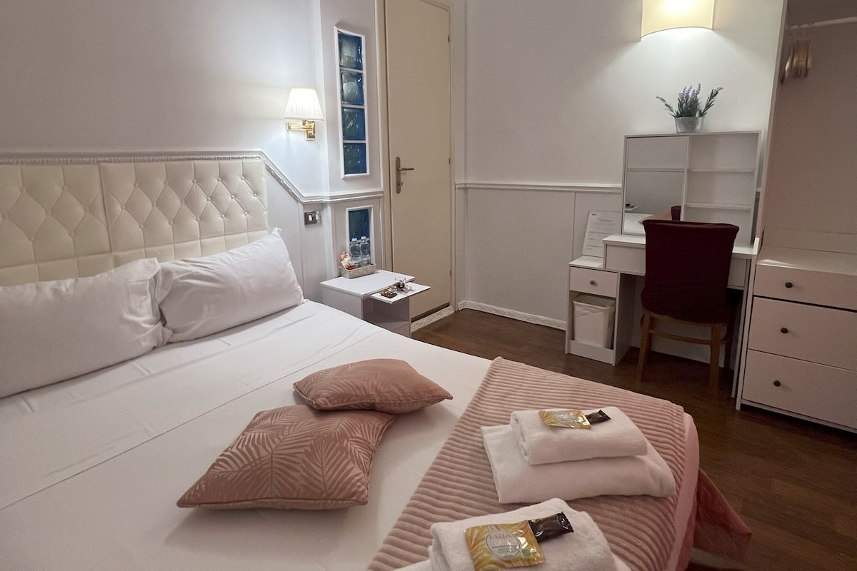 Quarto de hotel com uma cama grande, uma escrivaninha, uma cadeira e uma mesa de cabeceira.