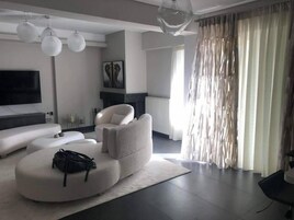 Uma sala de estar moderna com uma grande TV de tela plana, lareira e um espaço de estar confortável.