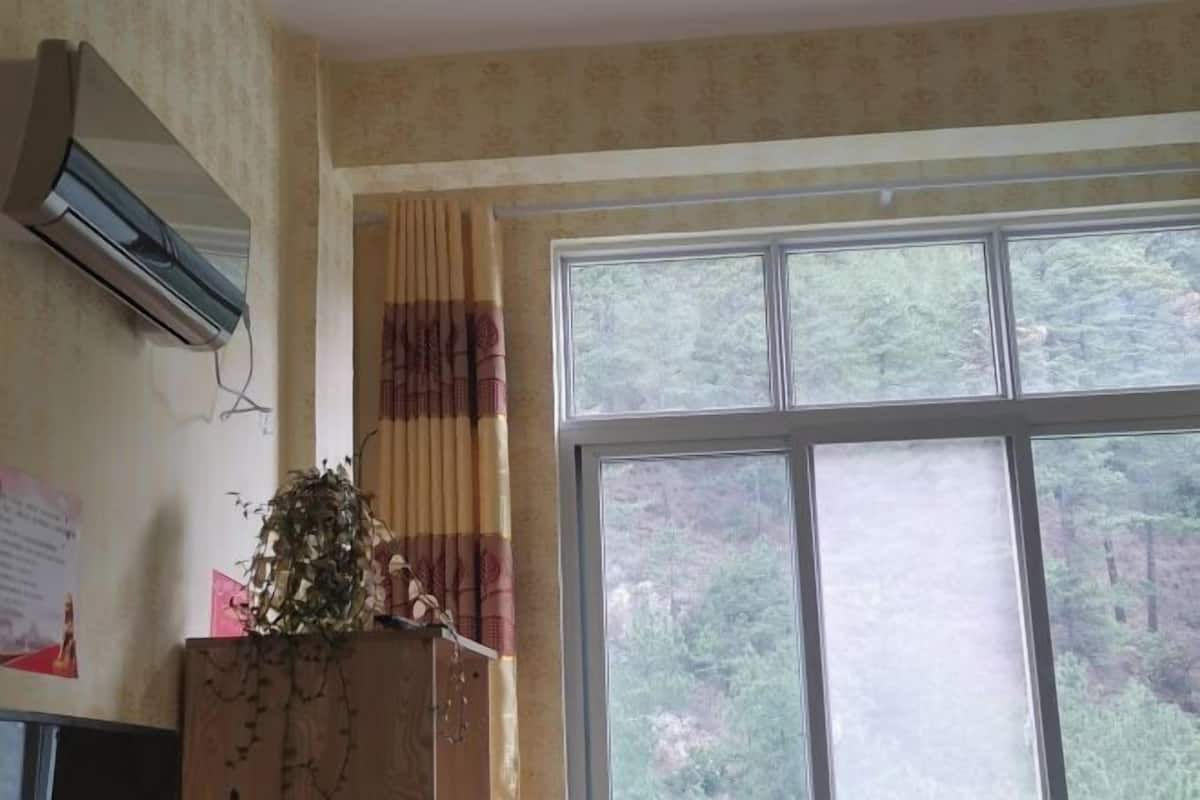 Quarto com uma janela ampla, uma escrivaninha de madeira e um aparelho de ar condicionado fixado na parede.