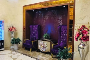 Uma área de recepção com disposição de assentos, um painel decorativo e plantas em vasos.