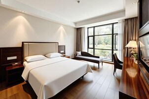Quarto de hotel com cama grande, escrivaninha, cadeira, sofá e televisão.