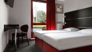 Quarto de hotel com cama, escrivaninha, cadeira e televisão.