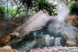 Uma área de águas termais com uma piscina de pedra cercada por pedras e vegetação.