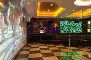 Um hall com piso xadrez, palco com tela grande e área de estar com parede estampada.