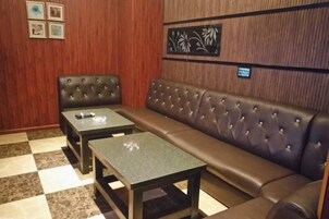 Quarto com sofá de couro marrom, duas mesas quadradas e piso xadrez.