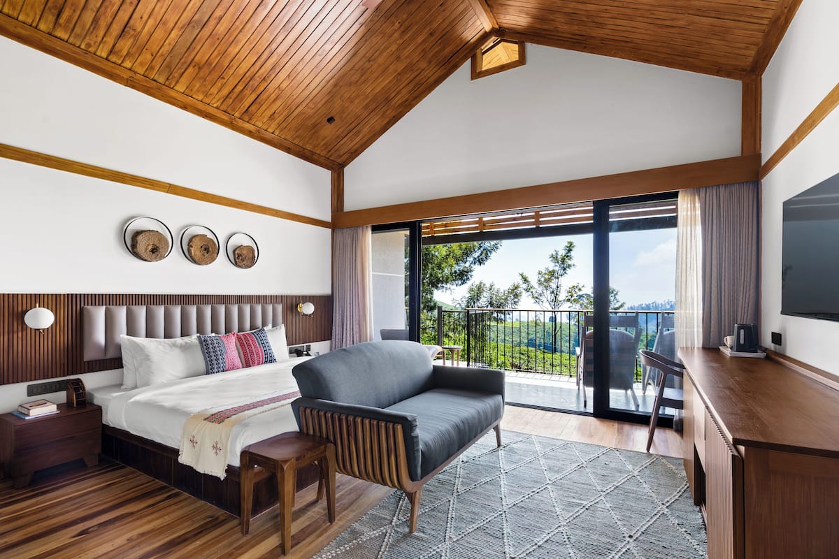 Quarto de hotel moderno com uma cama grande, sofá, escrivaninha e varanda com vista.