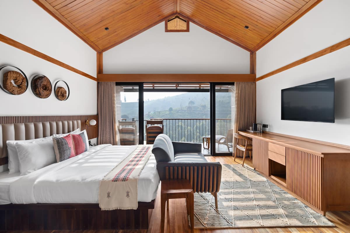 Quarto com cama grande, escrivaninha, televisão e varanda com vista.