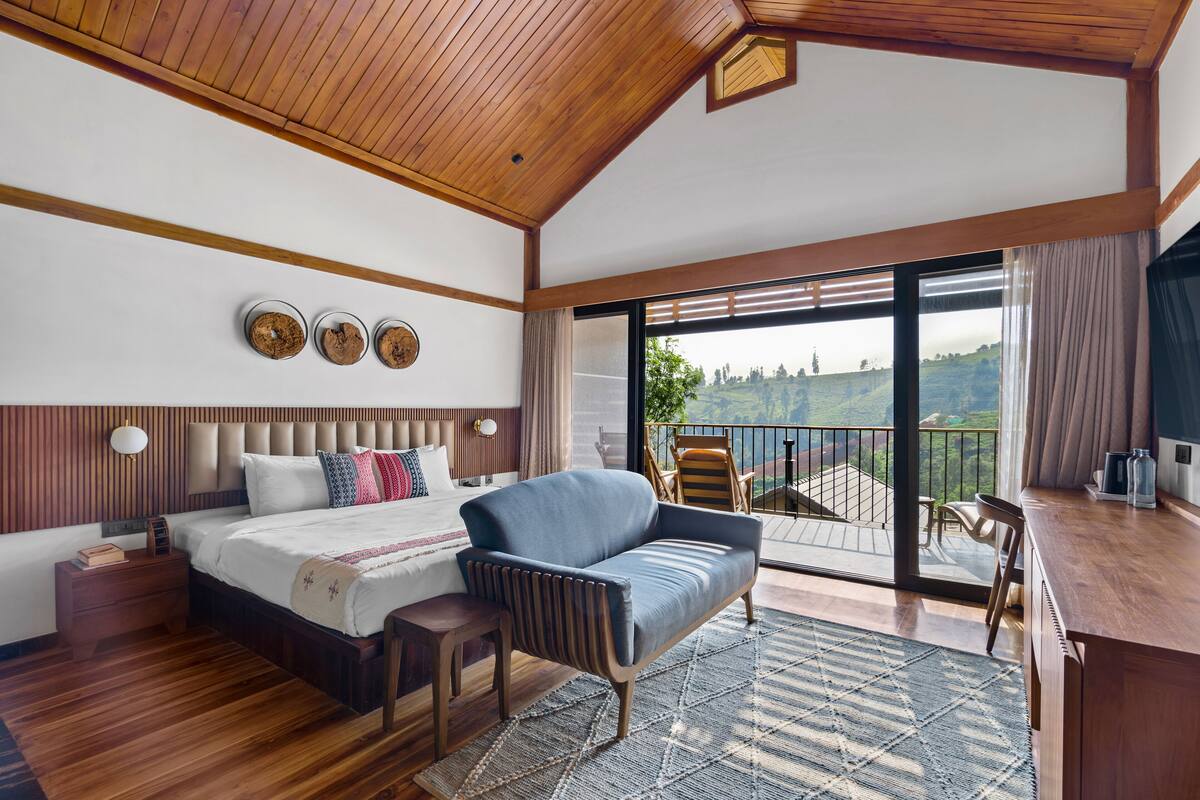 Quarto com cama grande, sofá, escrivaninha e varanda com vista.