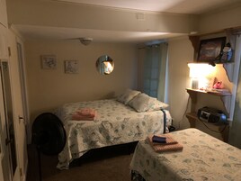 Quarto com duas camas, um ventilador de teto, um espelho e uma prateleira com objetos pessoais.