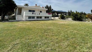 Uma casa moderna de dois andares com telhado plano, varanda coberta e gramado bem cuidado.