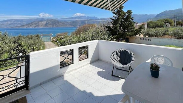 Uma varanda com vista para o mar e montanhas, uma mesa branca e um toldo listrado.