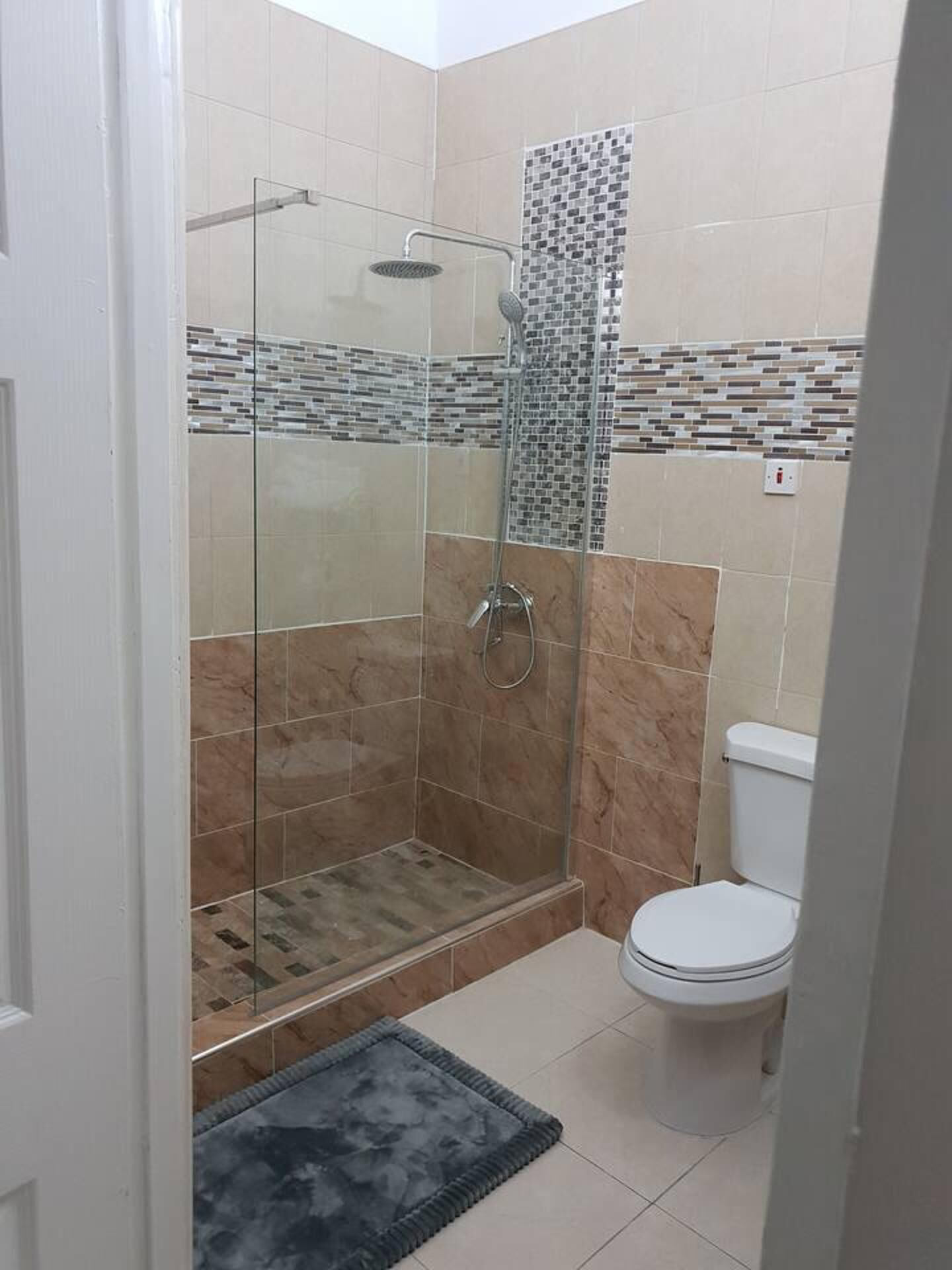 Casa de banho com cabine de duche em vidro, sanita e painel de azulejos estampados.