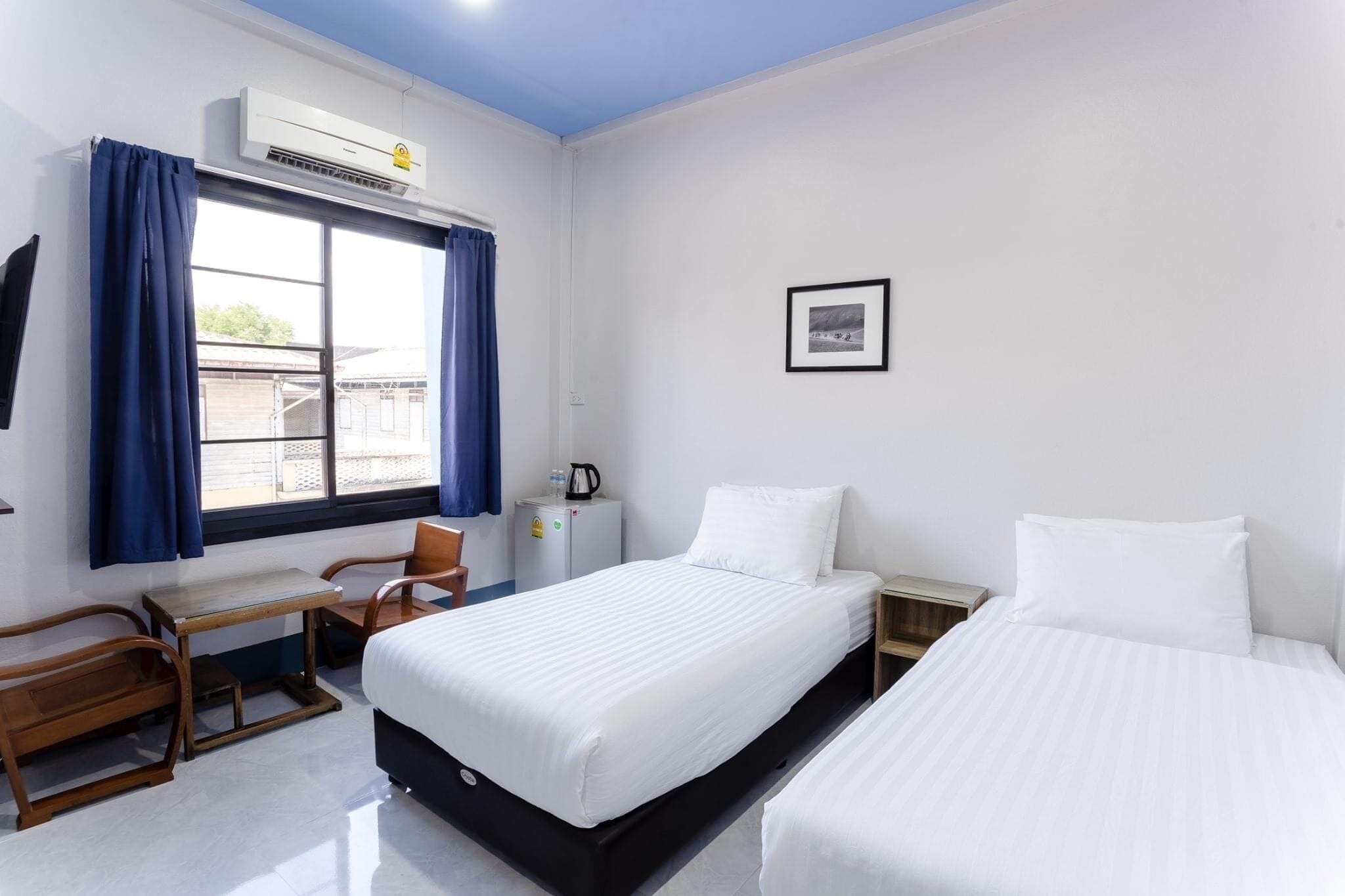 Quarto de hotel com duas camas, uma escrivaninha, uma cadeira, uma mesa pequena e um aparelho de ar condicionado.