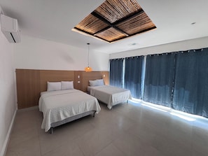 Quarto de hotel moderno com duas camas, cabeceira de madeira, uma janela grande com cortinas e um lustre no teto.