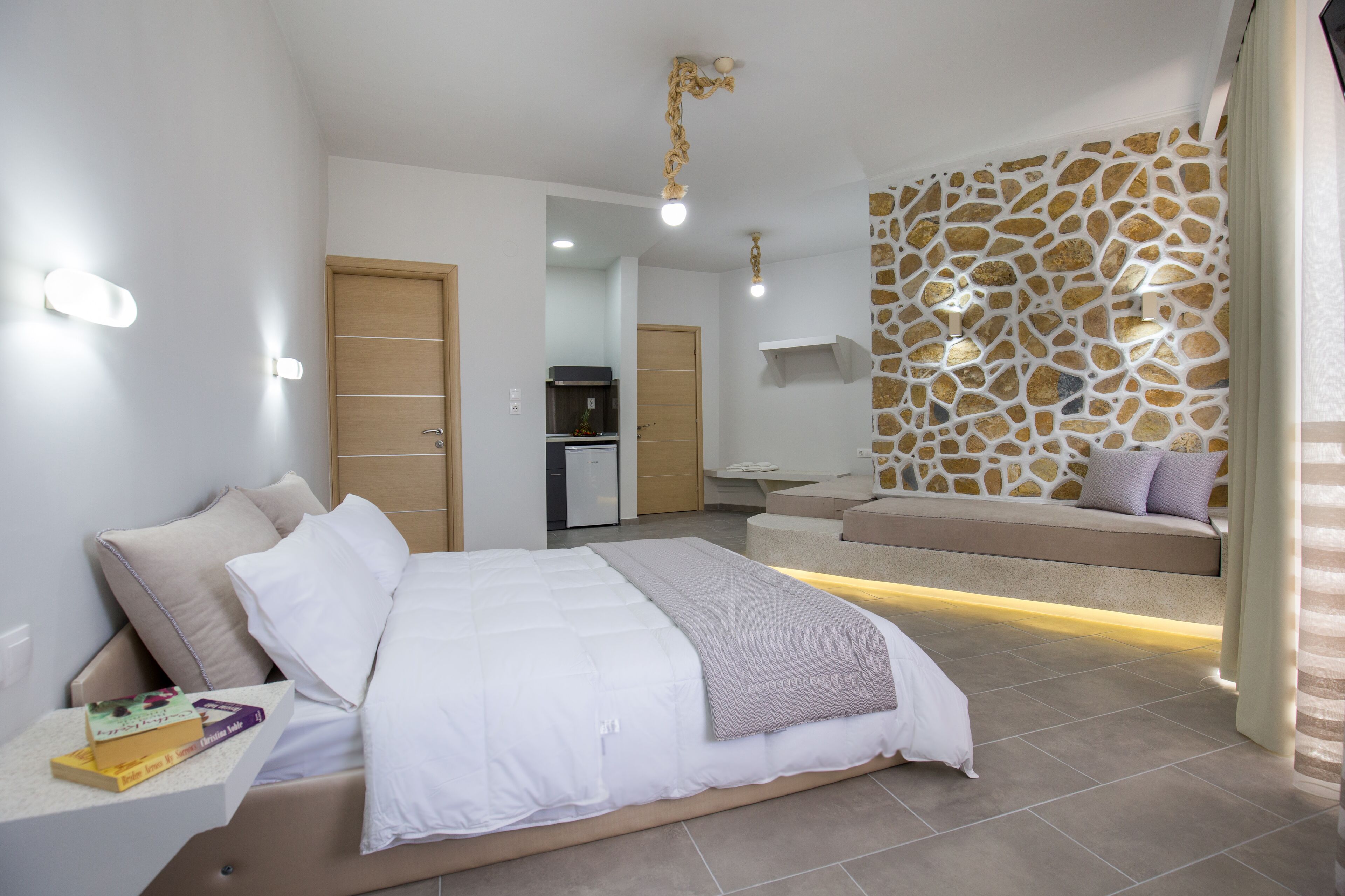 Quarto moderno com cama, mesas de cabeceira, parede de pedra e um banco embutido.