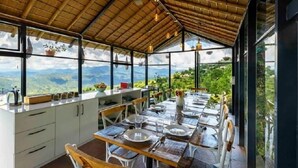 Uma área de refeições com teto alto, janelas amplas e vista para as montanhas.