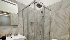 Um banheiro moderno com chuveiro em box de vidro, pia branca com artigos de higiene pessoal e vaso sanitário.