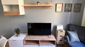 Uma sala de estar moderna com uma televisão de tela plana, um armário branco, um sofá cinza e uma estante de madeira com objetos decorativos.