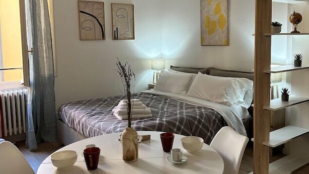 Quarto moderno com cama, mesa de cabeceira e um pequeno espaço de refeições com mesa e cadeiras.