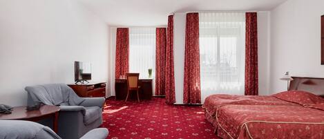 Quarto de hotel com carpete vermelho, duas camas, uma escrivaninha com cadeira, um sofá e uma televisão.