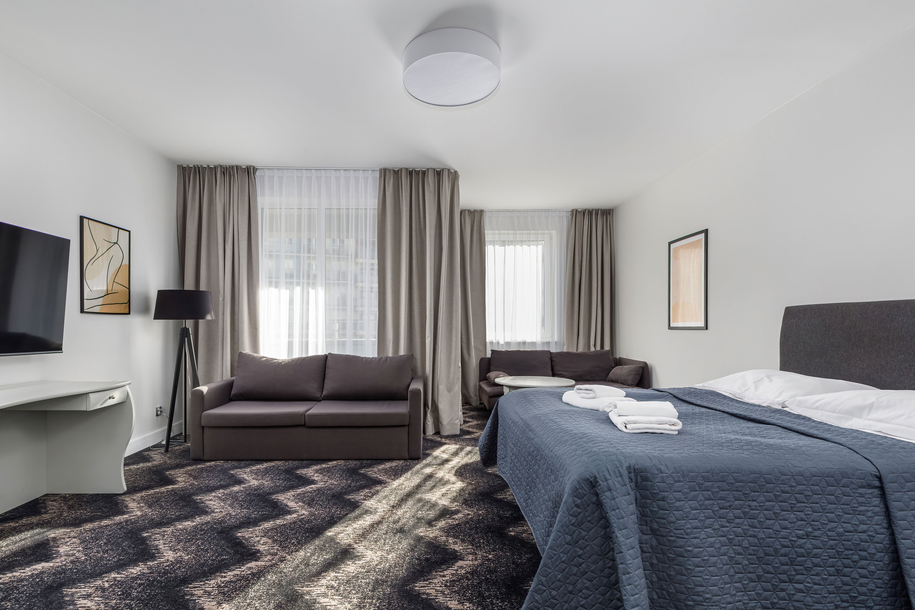 Quarto de hotel moderno com cama, sofá, escrivaninha e televisão.