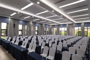 Uma sala de conferências com fileiras de mesas e cadeiras, janelas amplas e um design moderno no teto.
