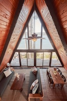 Um quarto amplo com pé direito alto, uma grande janela com vista para a água, móveis de madeira e um ventilador de teto.