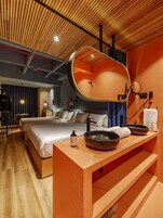 Quarto de hotel moderno com uma cama grande, teto de madeira e banheiro com um espelho amplo e duas bacias na pia.