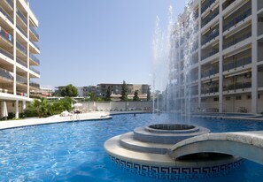 Piscina com uma fonte, rodeada por um edifício branco com varandas.
